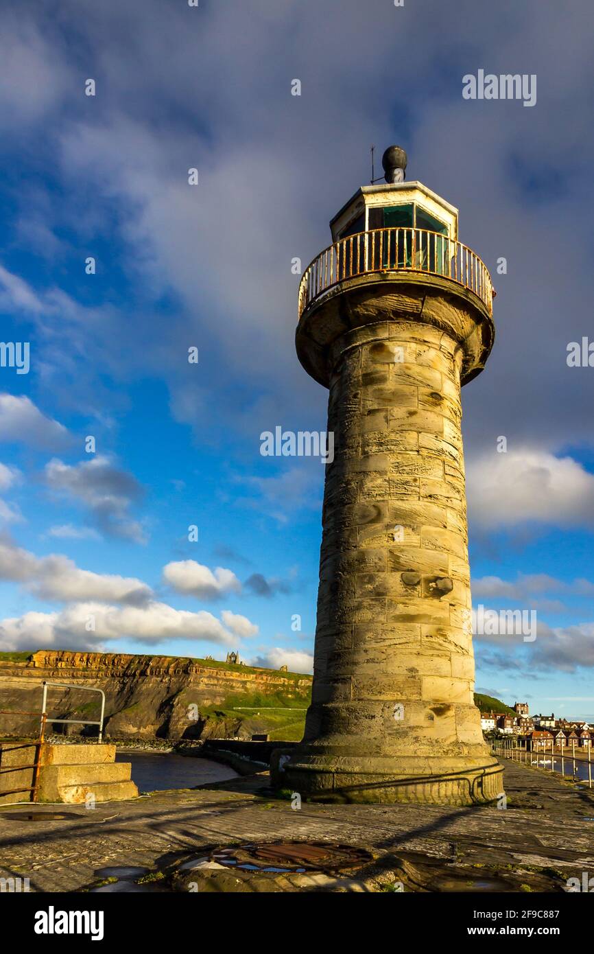 Whitby harbour lighthouse in summer with blue sky and golden sun ...