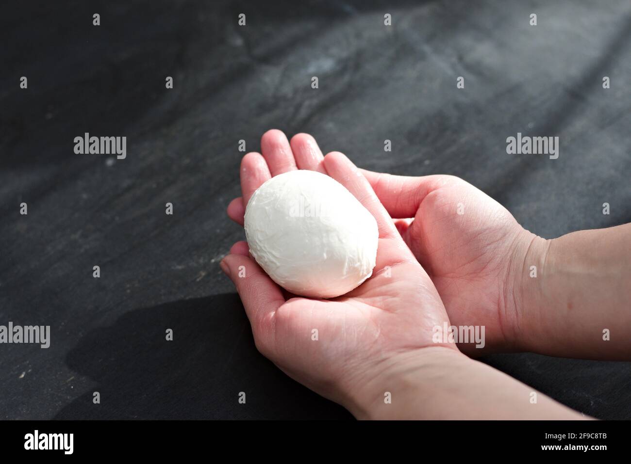 Lump of freshly made mozzarella cheese in female hands on black ...