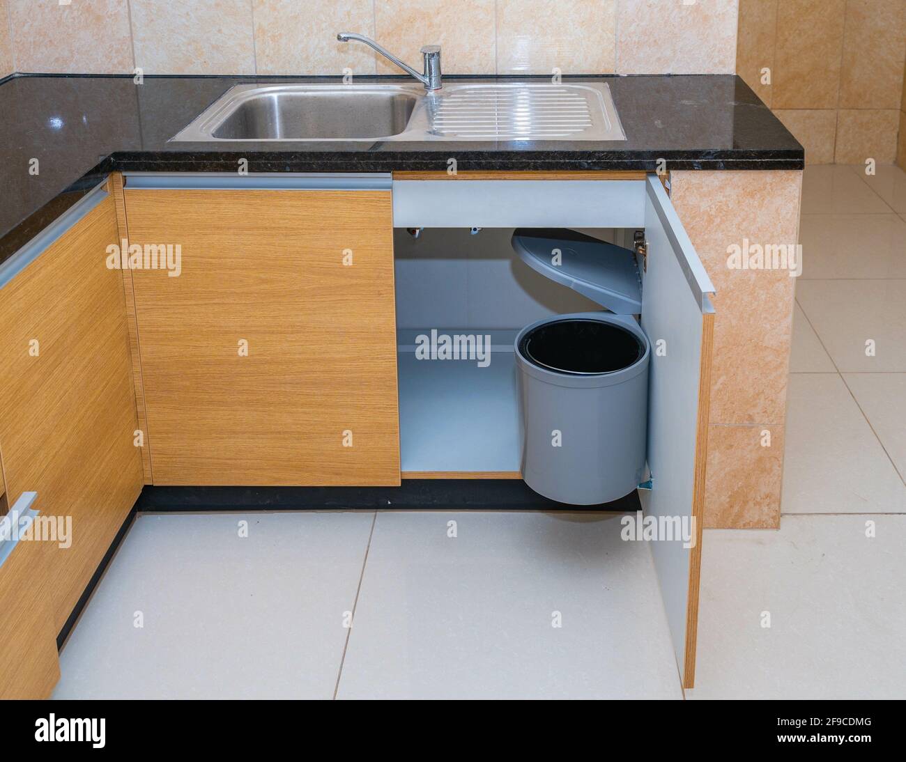 Closeup of the opened kitchen sink cabinet with a plastic trashcan ...