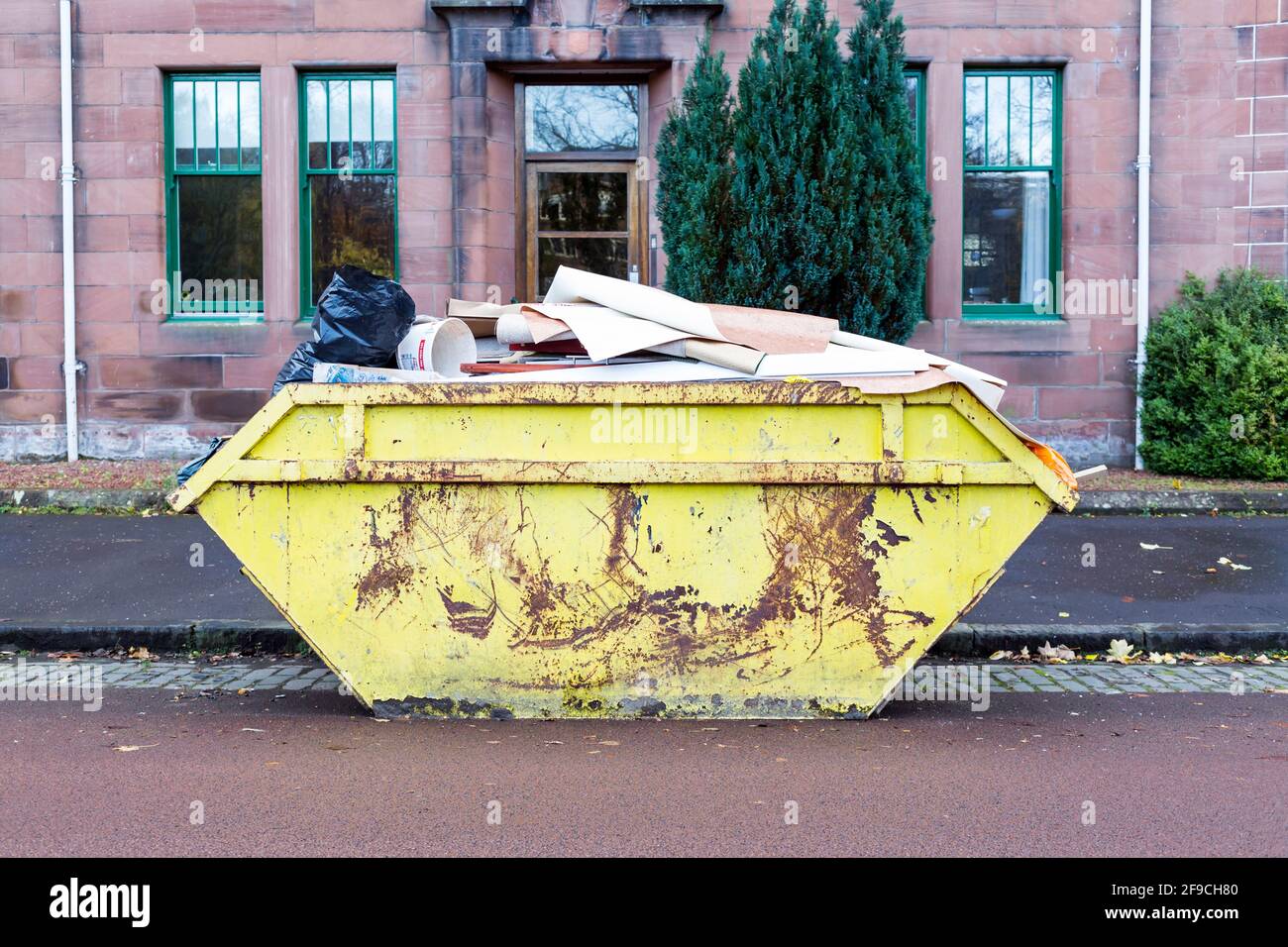 Skip full of building waste on a road outside a tenement building, UK ...
