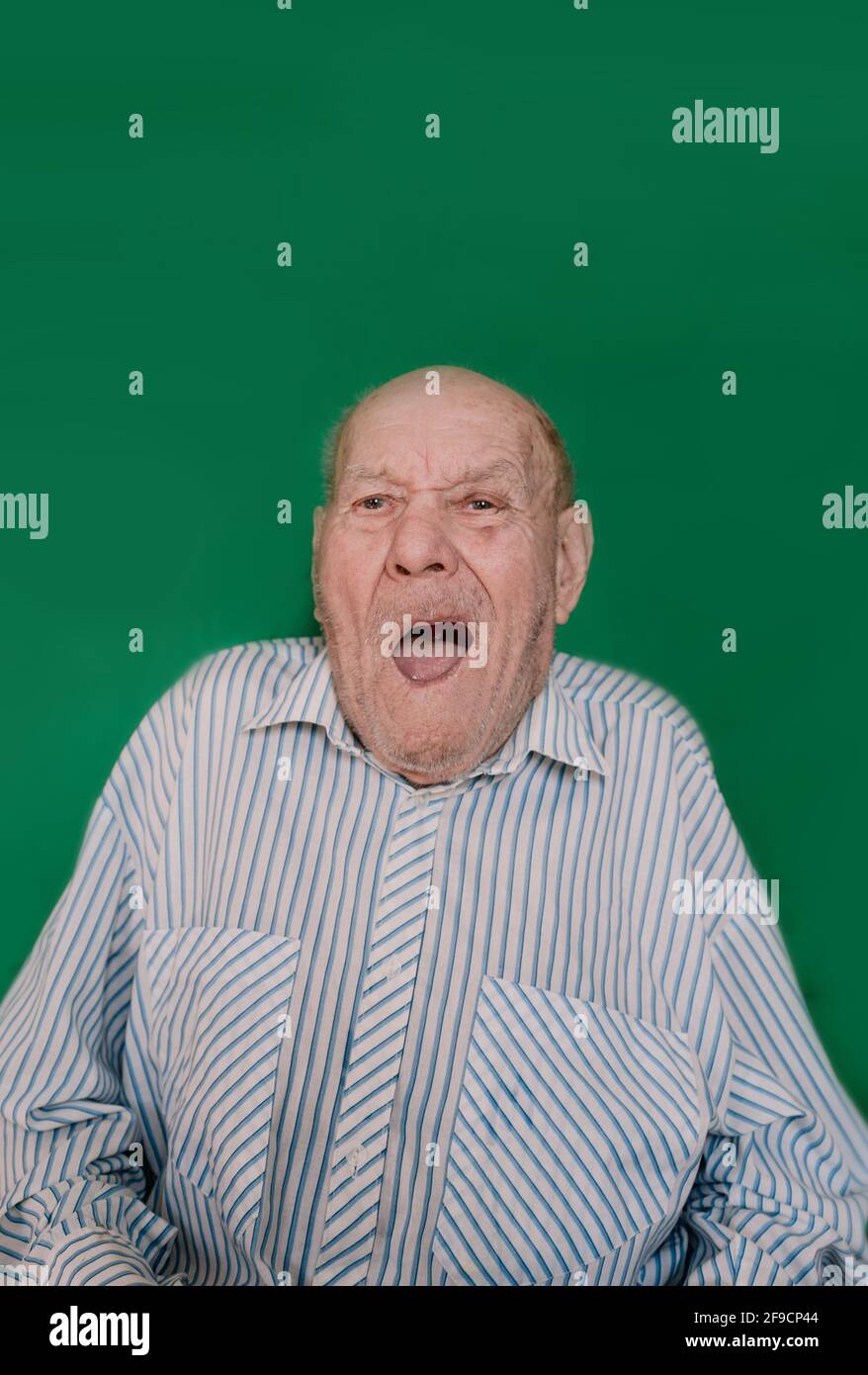 a crazy old man makes faces and grimaces against an isolated green ...