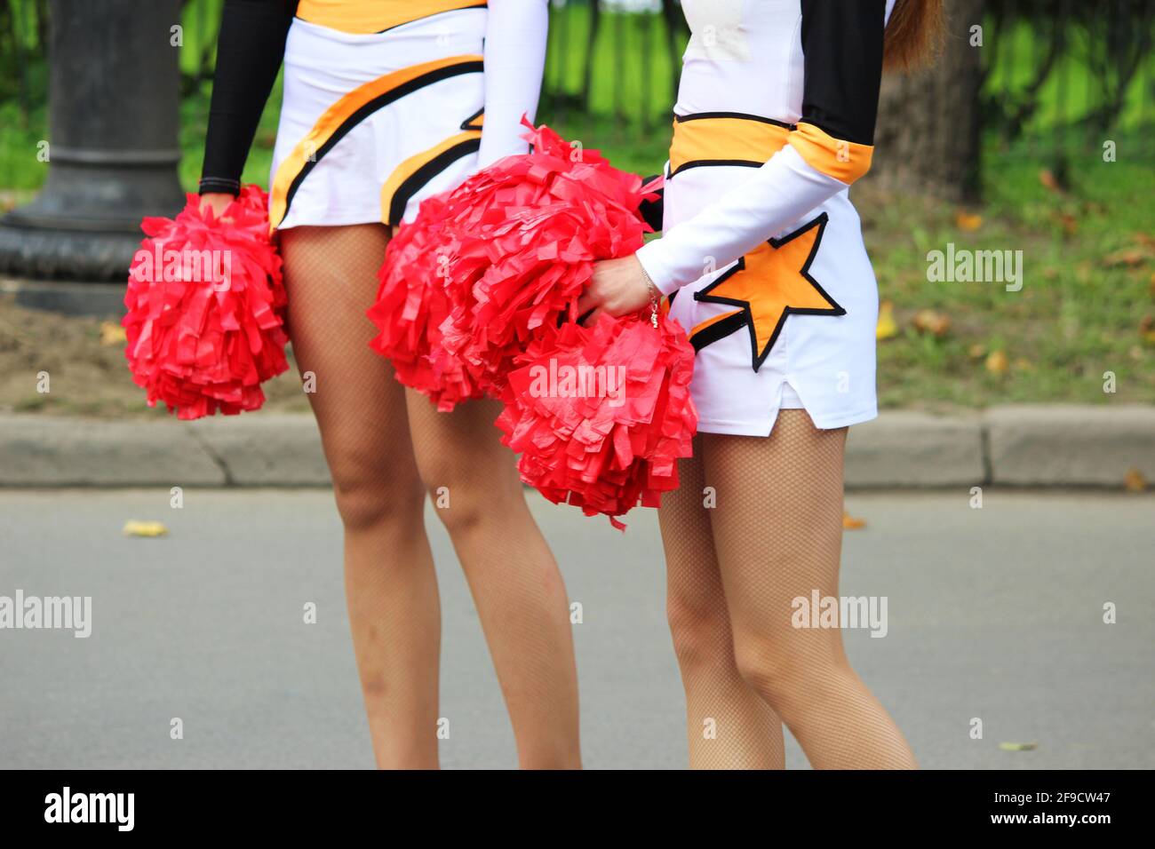 two girls from the cheerleading team stand outside with red pompoms in ...