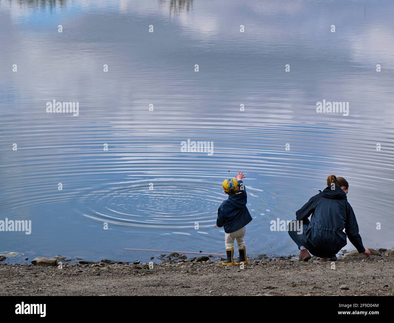 Small child throwing stones in a lake as the mother collects stones ...
