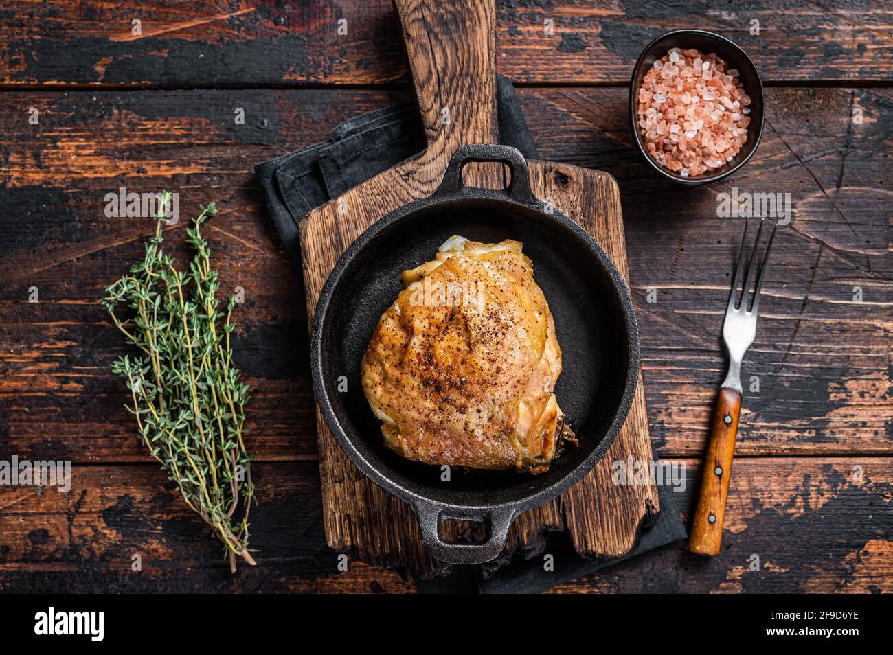 Baked chicken thigh in a pan with rosemary and salt. Dark wooden ...