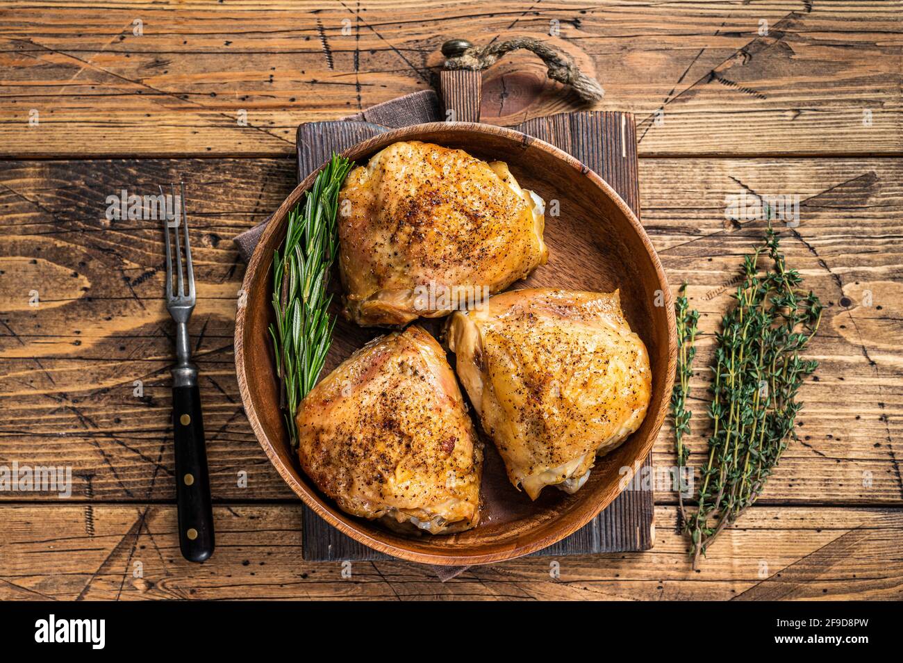 Roasted chicken thighs in a wooden plate with rosemary and herbs ...