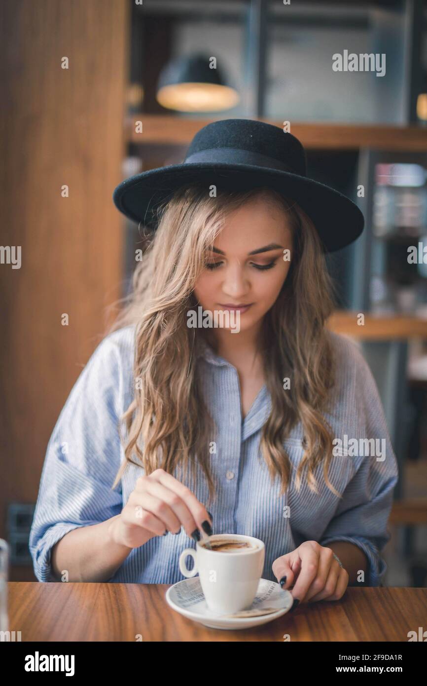 Shallow focus of a Caucasian woman with a fedora hat drinking coffee in ...