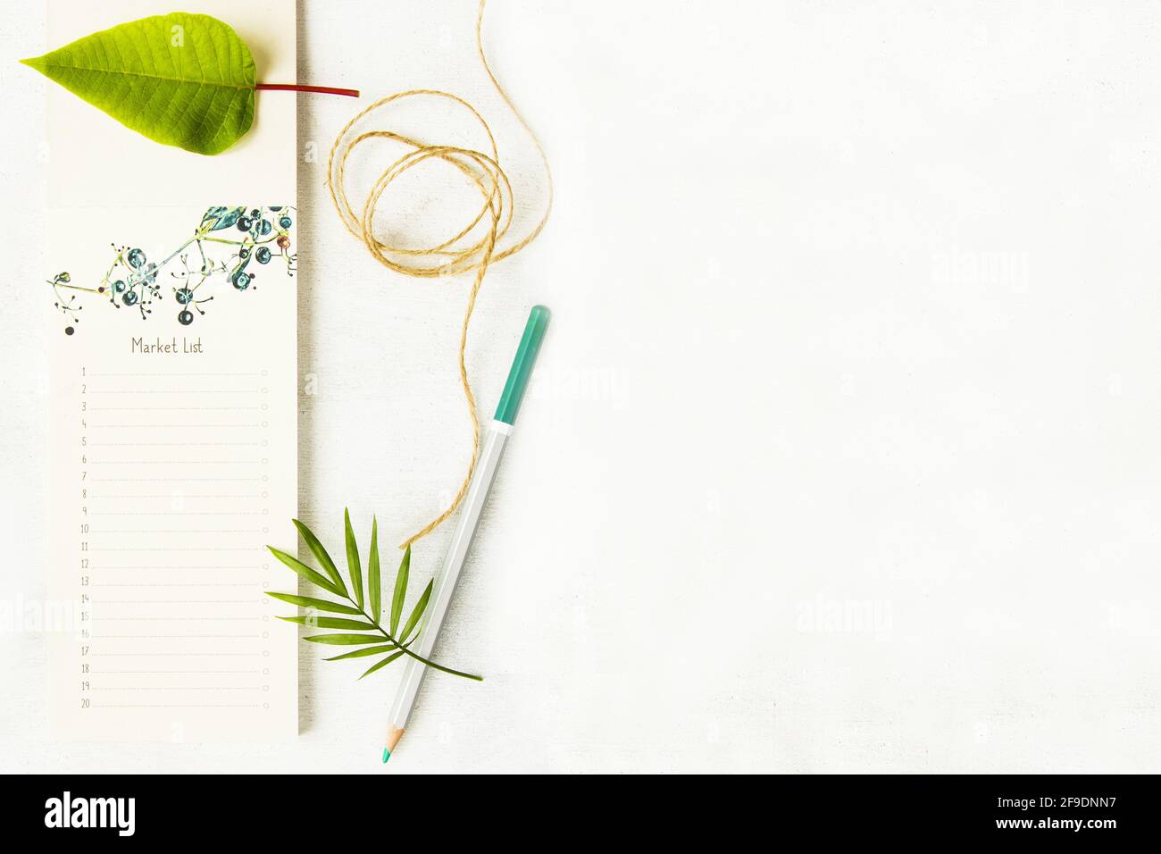A top view of a blank market list with a pencil and plants against a ...