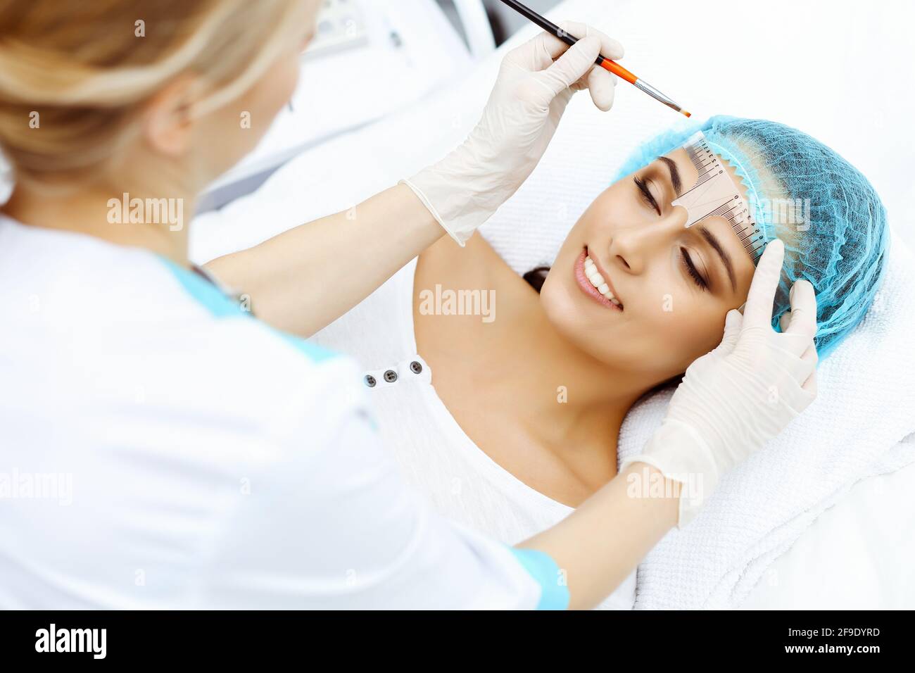 Professional beautician is going to correct eyebrow line at woman face ...