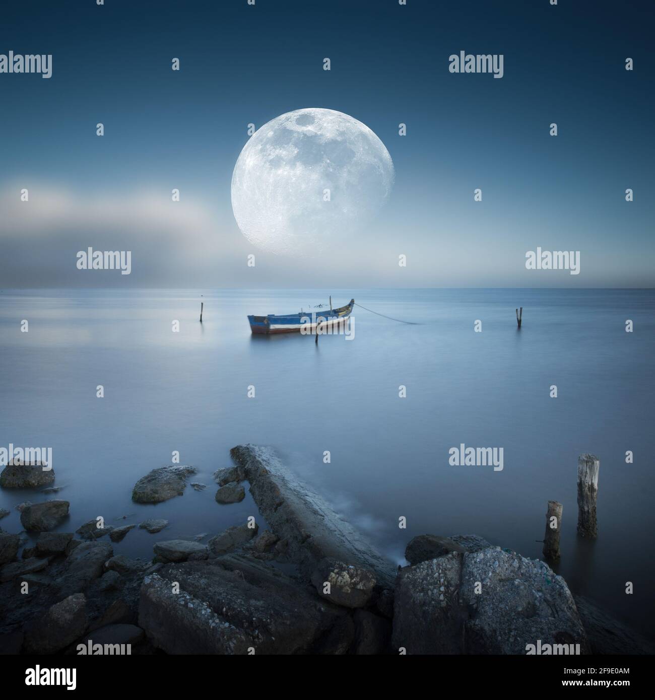The full moon on a blue sky above the sea with long exposure and a boat ...