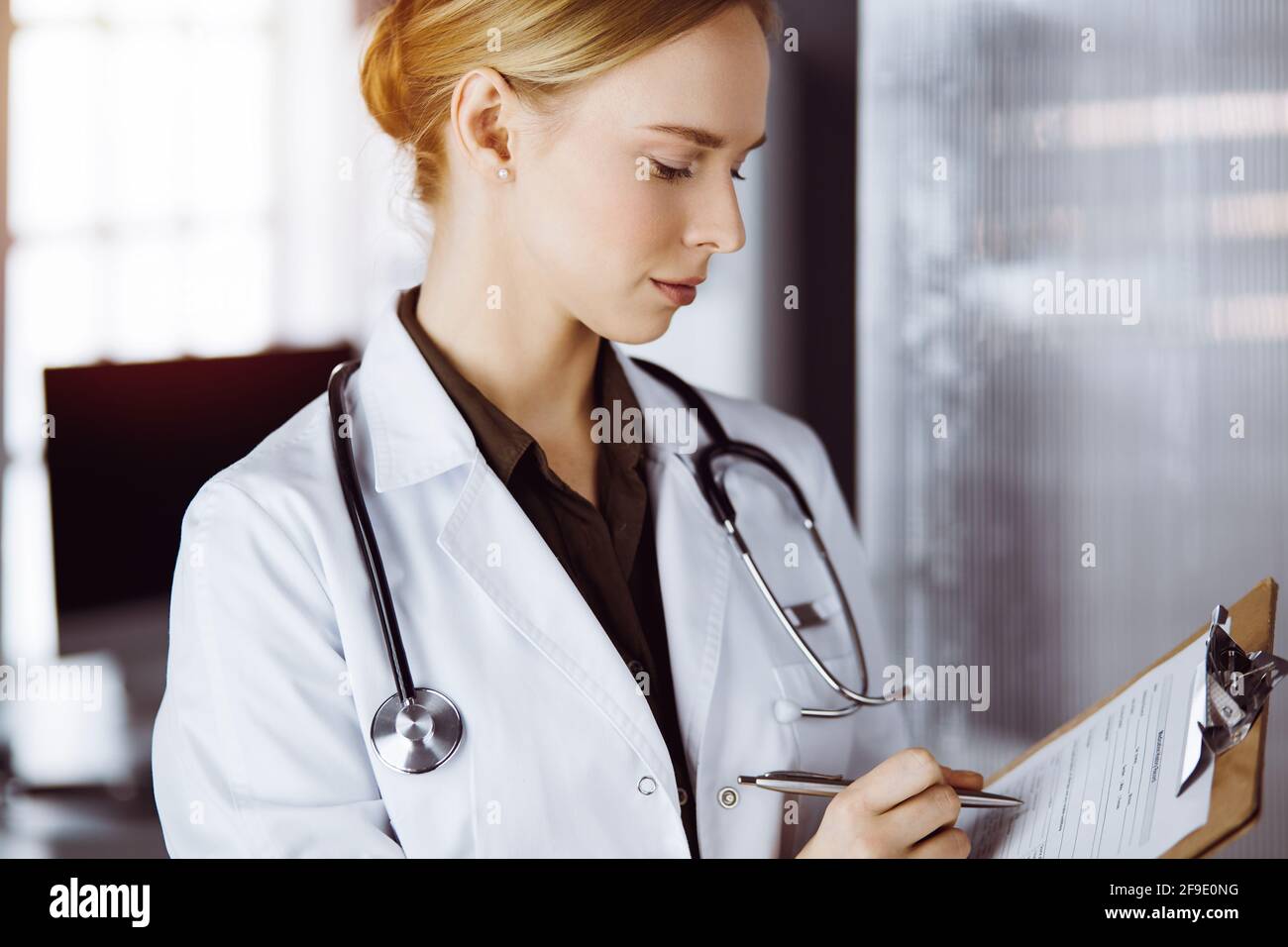 Cheerful smiling female doctor using clipboard in clinic. Portrait of ...