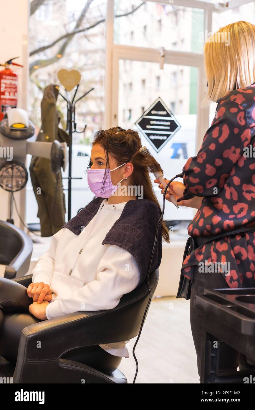 A Caucasian hairdresser with a protective mask performing a hairstyle ...
