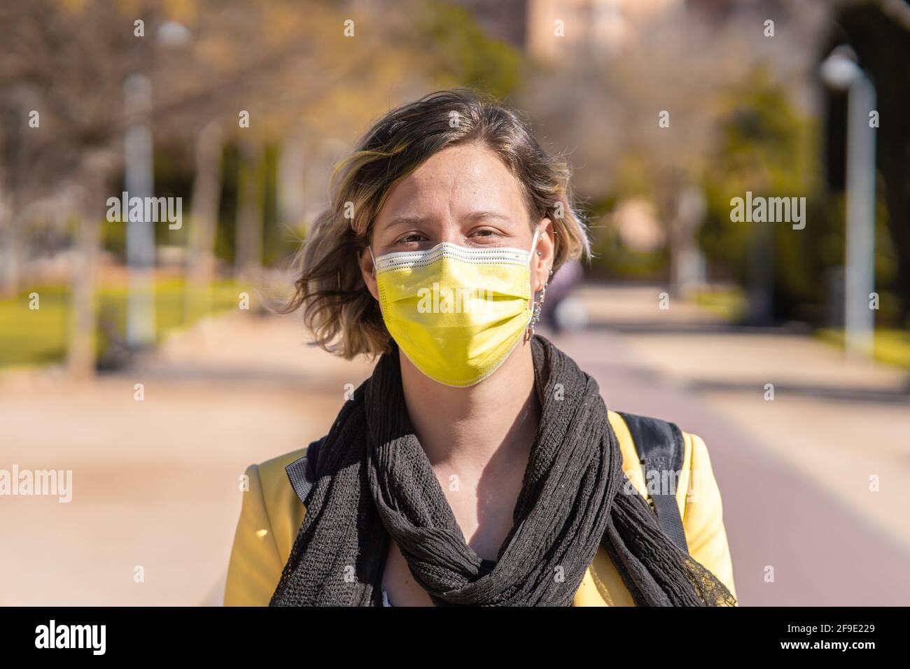 A shallow focus of a Spanish woman wearing a yellow face mask outdoors ...