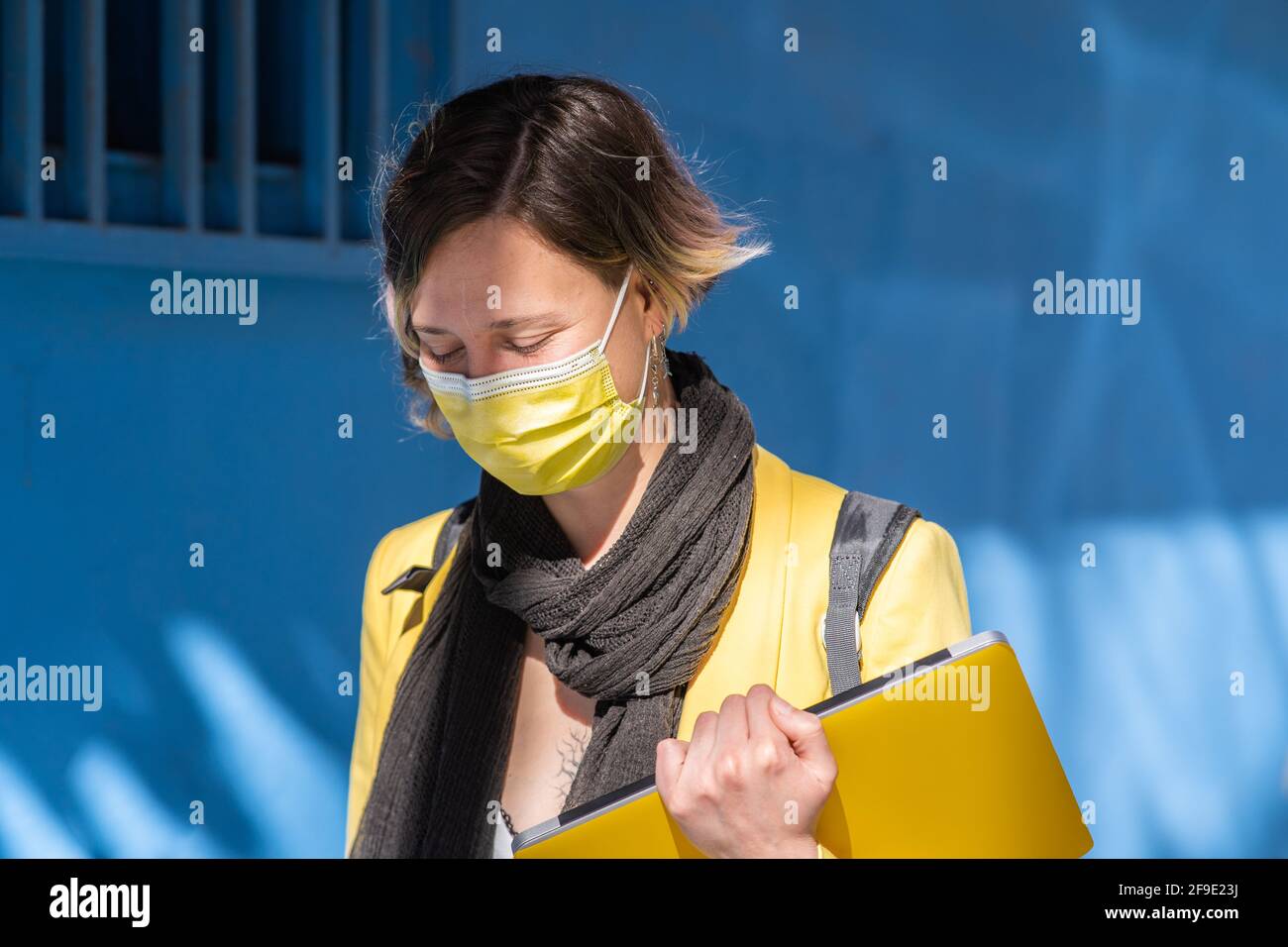 A young Caucasian female with a mask holding a yellow laptop against a ...