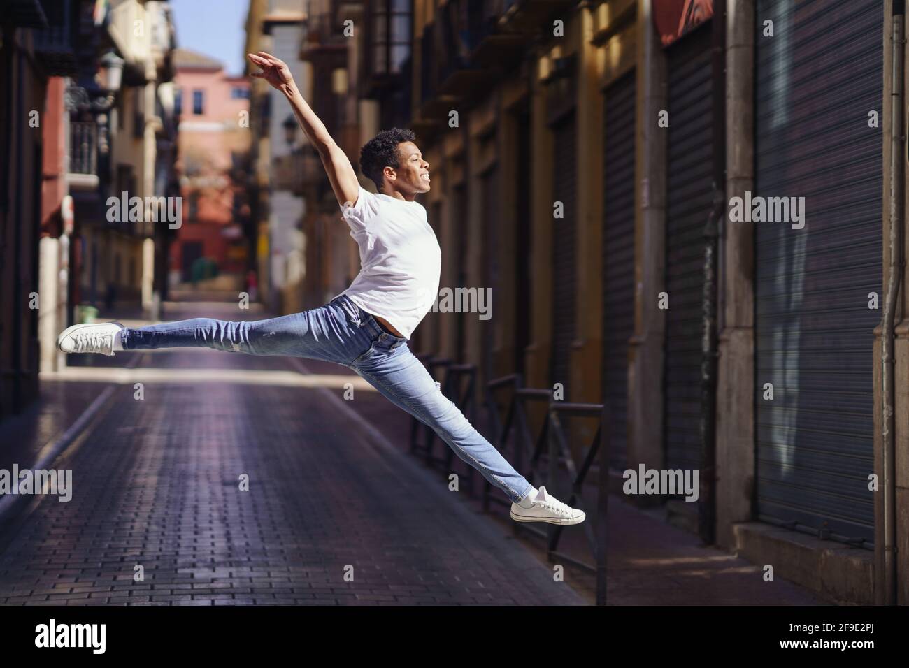 Happy black guy doing an acrobatic jump in the middle of the street ...