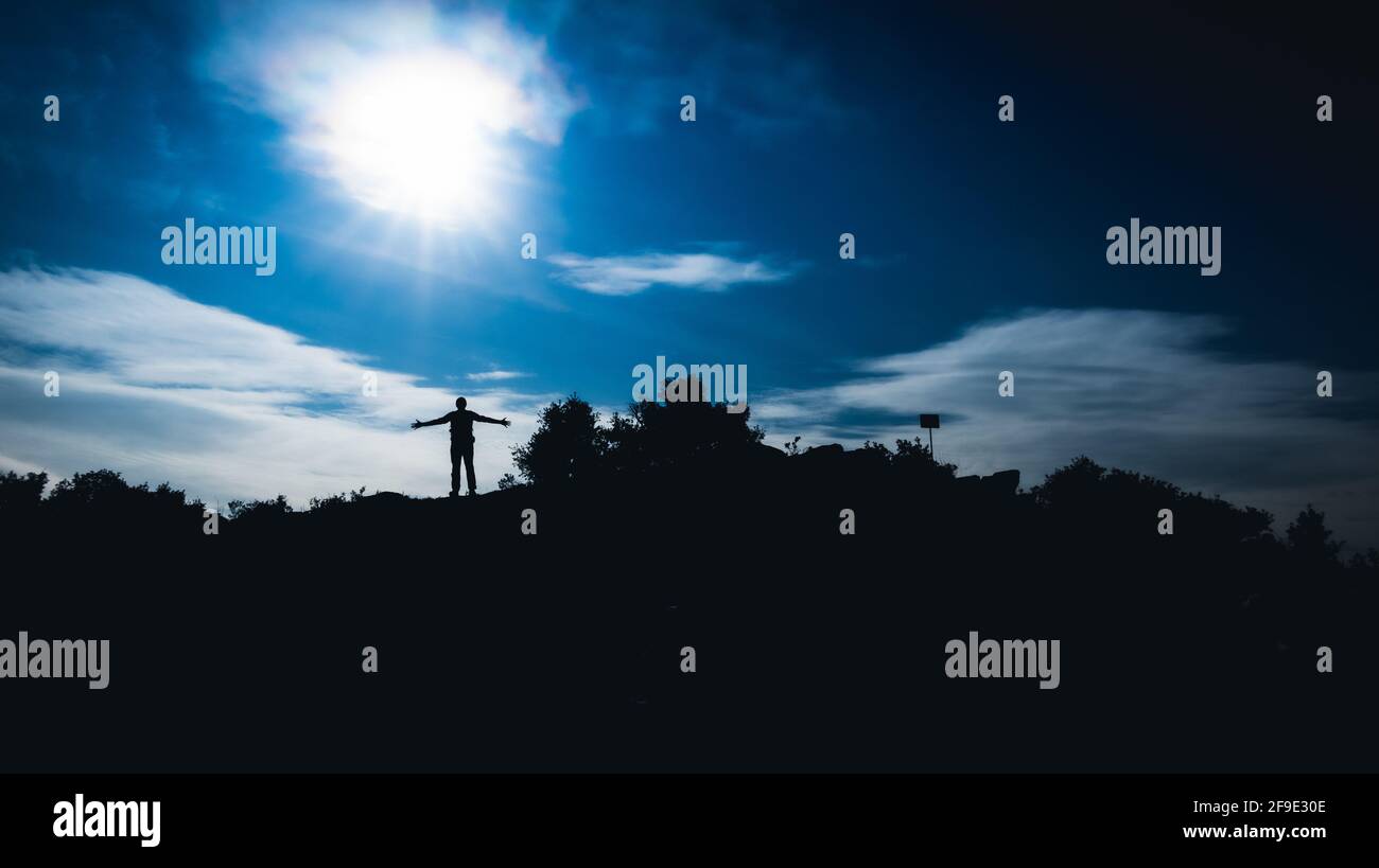 A silhouette of a man with wide-open hands standing on the top of a ...