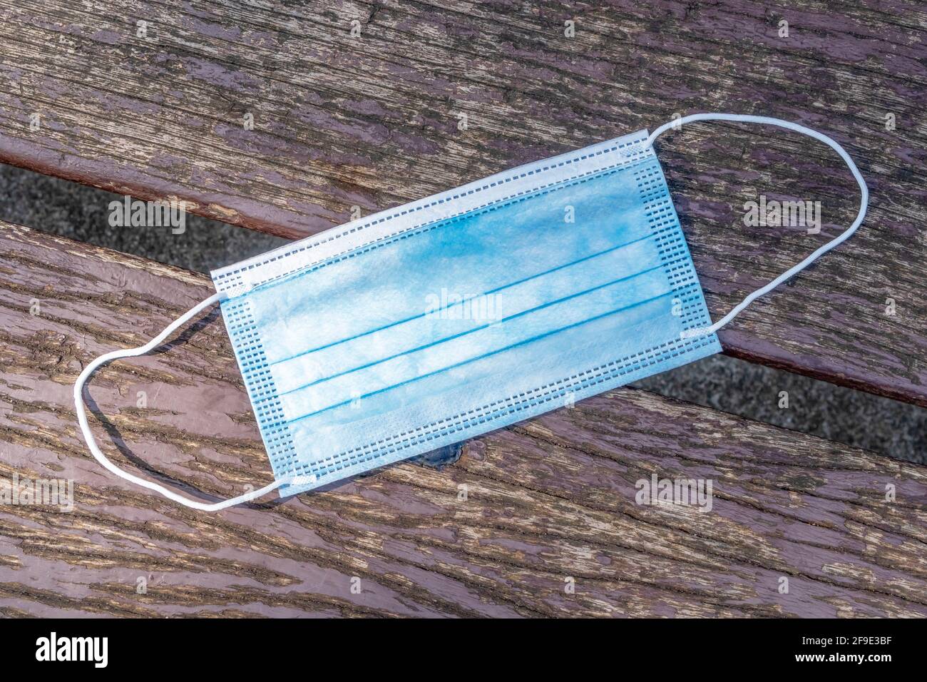 A used discarded surgical mask on a cracked wooden bench. Close-up ...