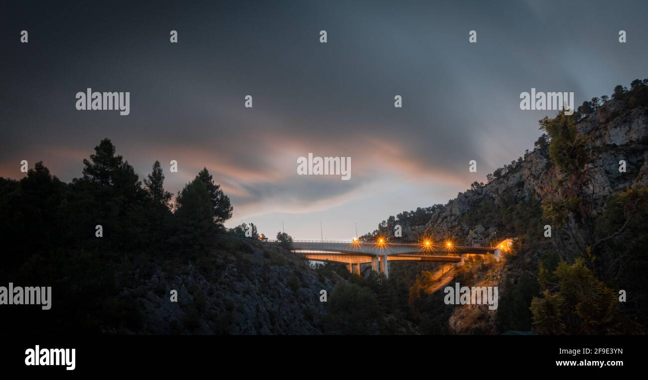 A beautiful nightscape of a lit bridge connecting tworocky mountains ...