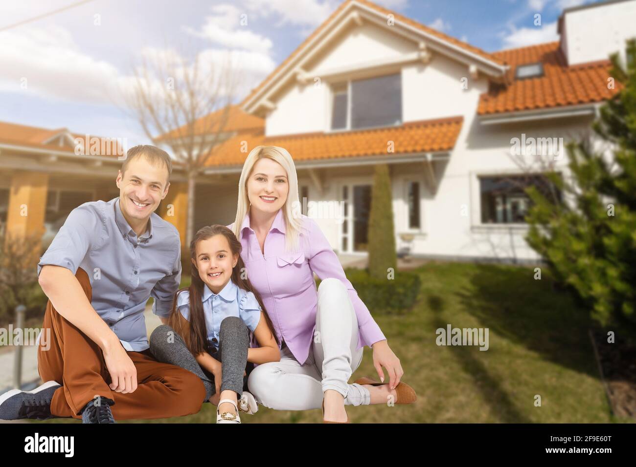 Family sitting on lawn in backyard, big modern house on background ...