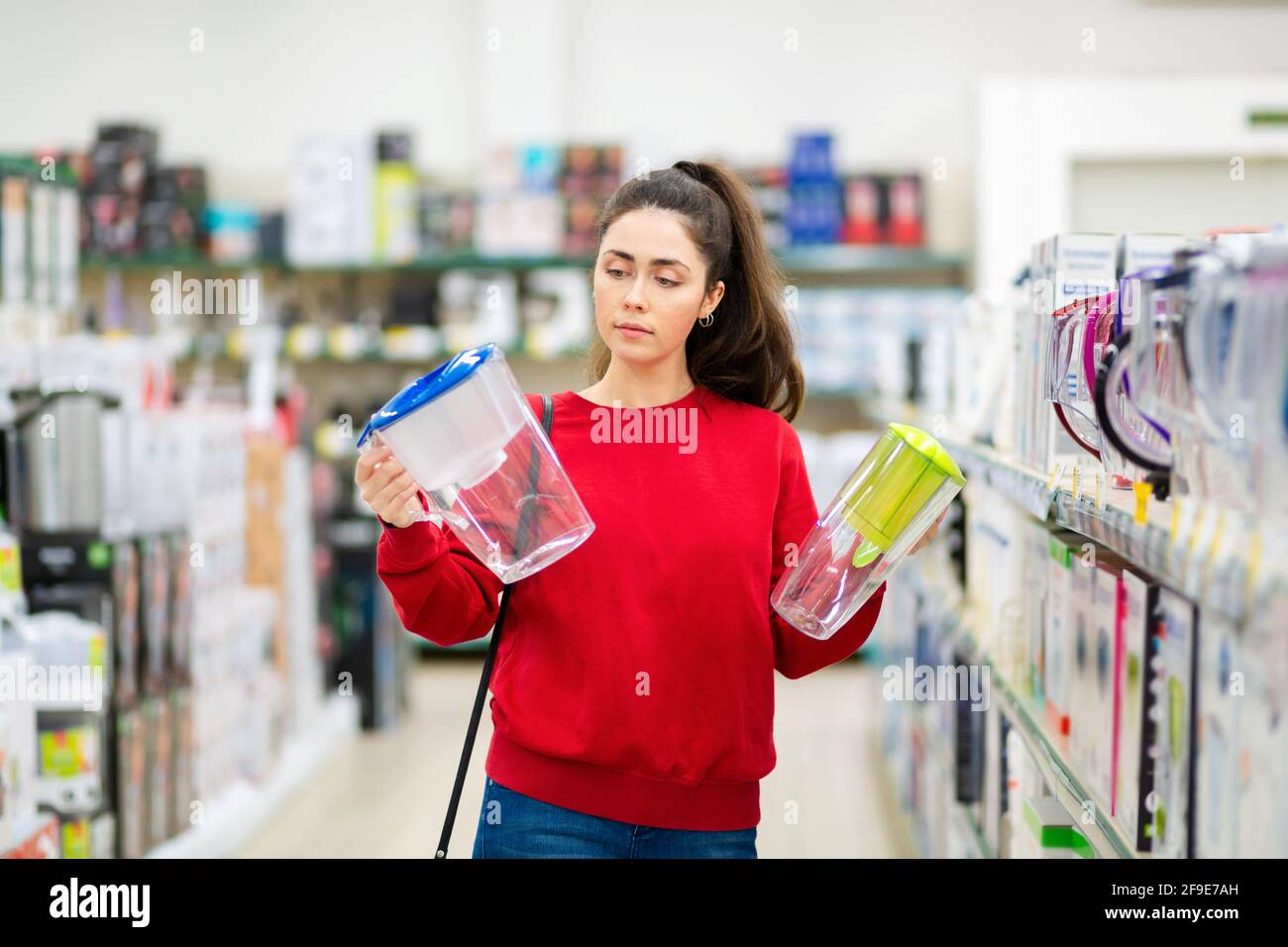 A young caucasian woman chooses between two carafe with a water filter ...