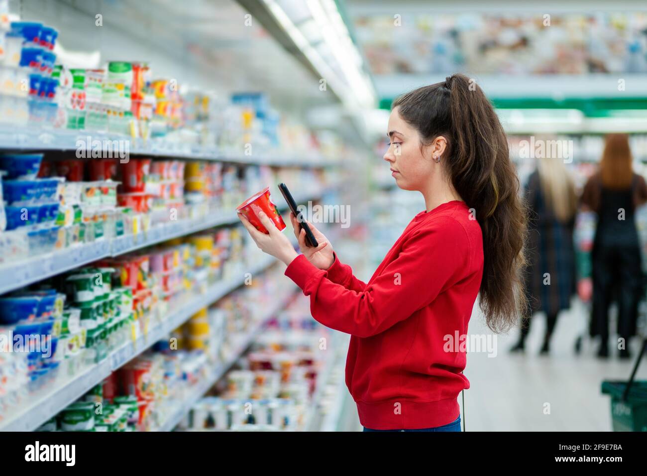 Portrait of young woman scans the QR code on a package of yogurt. In ...