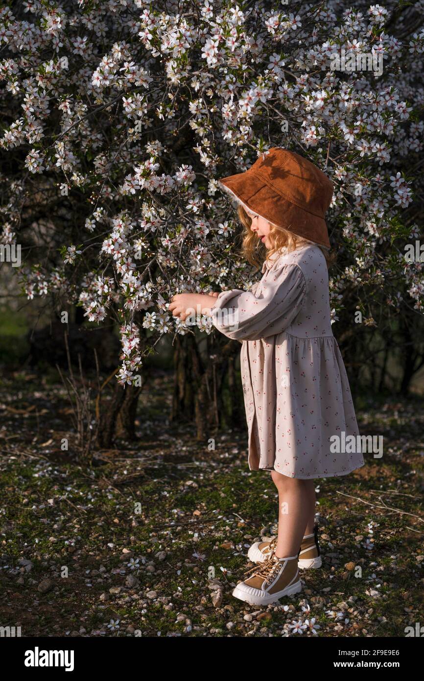 Adorable smiling little child in dress standing near blossoming tree ...