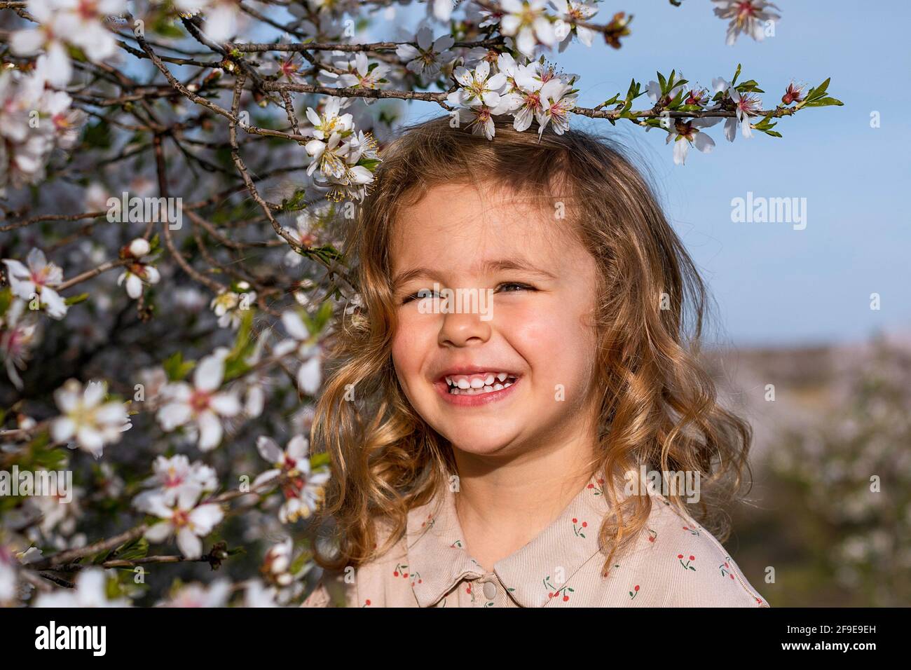 Adorable smiling little child in dress standing near blossoming tree ...