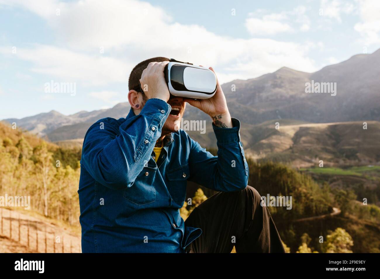 Curious male traveler sitting on hill and experiencing virtual reality ...