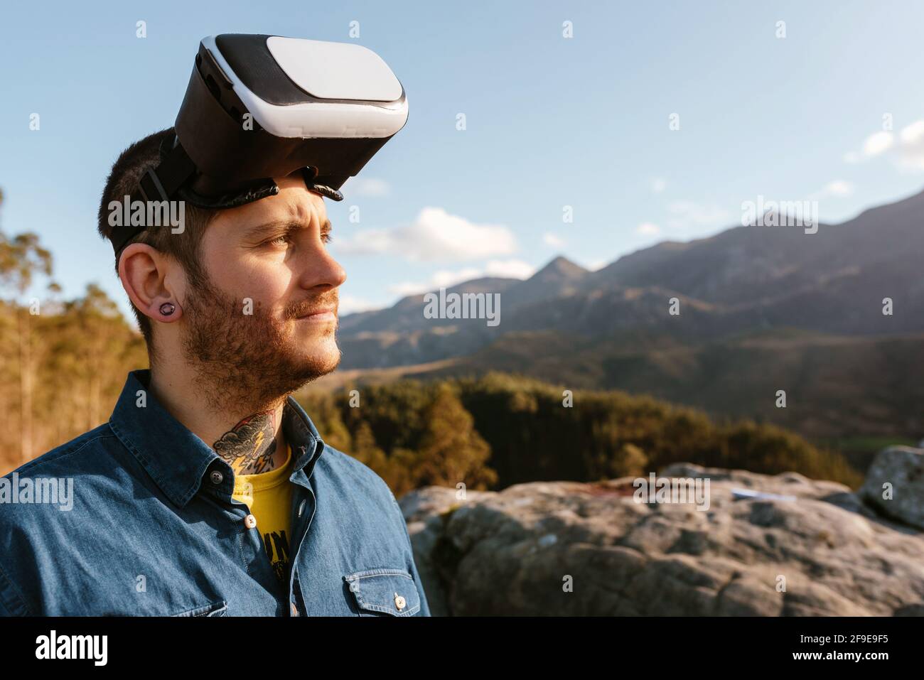 Curious male traveler sitting on hill and experiencing virtual reality ...