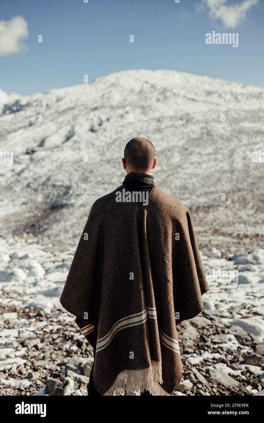Back view of anonymous male tourist in cape admiring snowy mount under ...