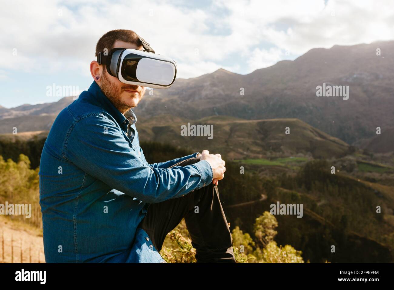 Curious male traveler sitting on hill and experiencing virtual reality ...
