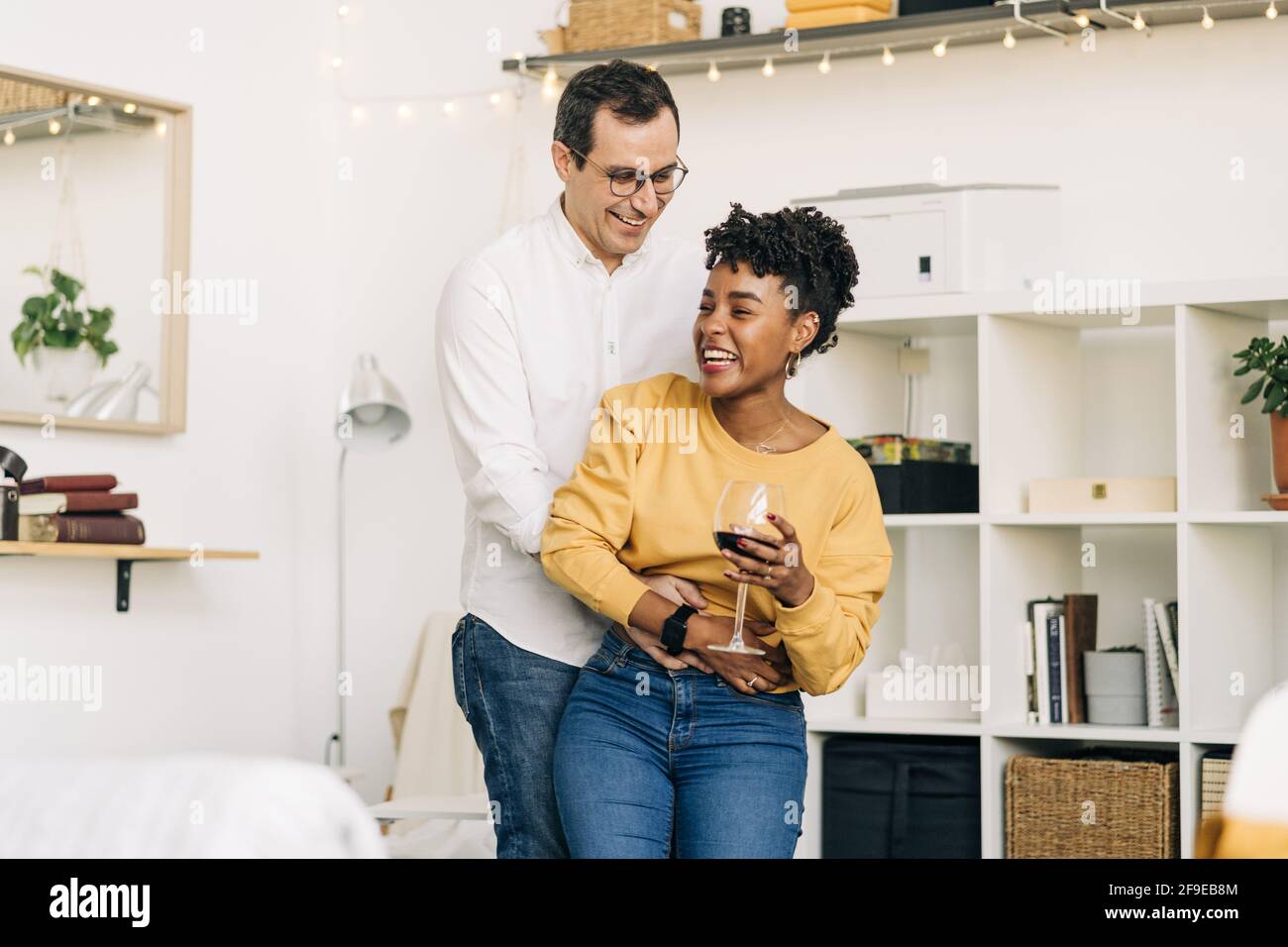 Delighted multiracial couple dancing in living room while spending time ...