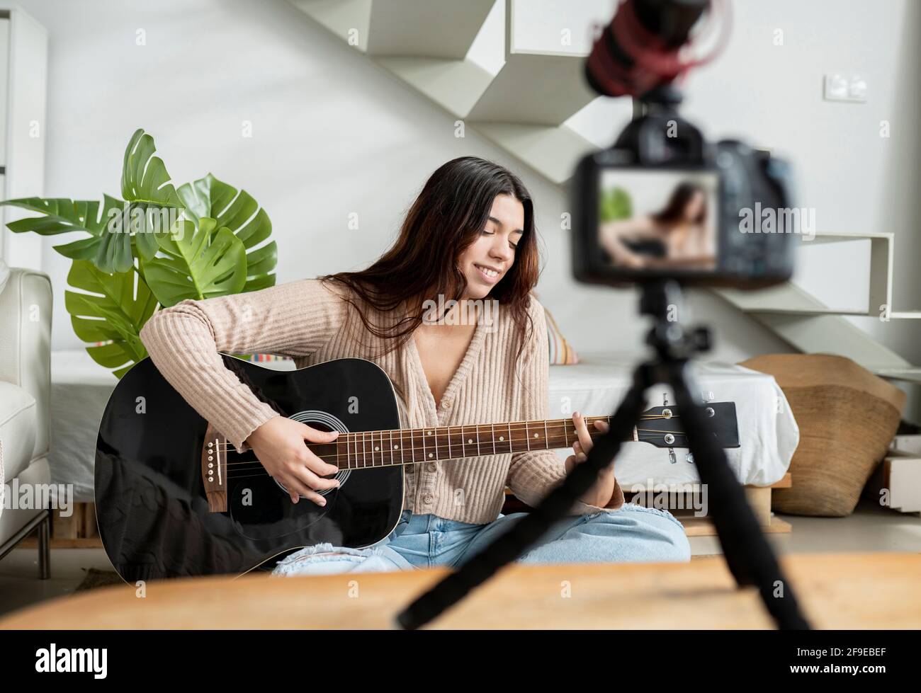 Photo of a woman playing an acoustic guitar while sitting by a window ...