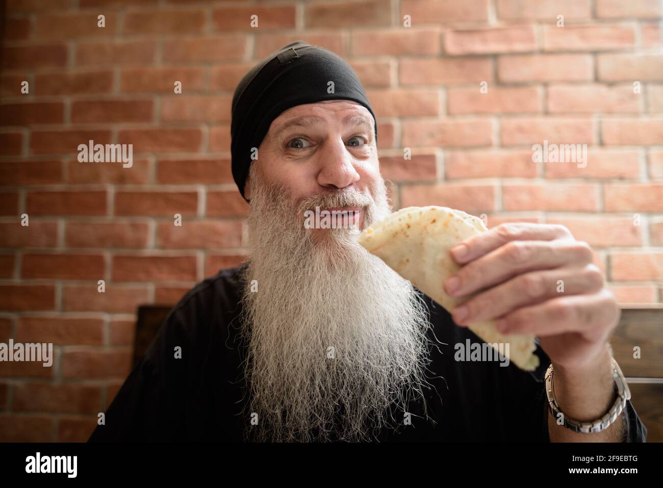 Man smiling with long gray beard while holding taco at restaurant Stock ...
