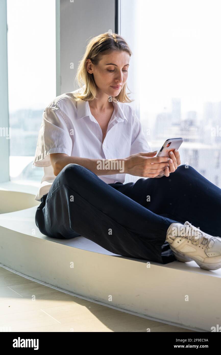 Lonely unemotional young Woman sitting in empty office with big window ...
