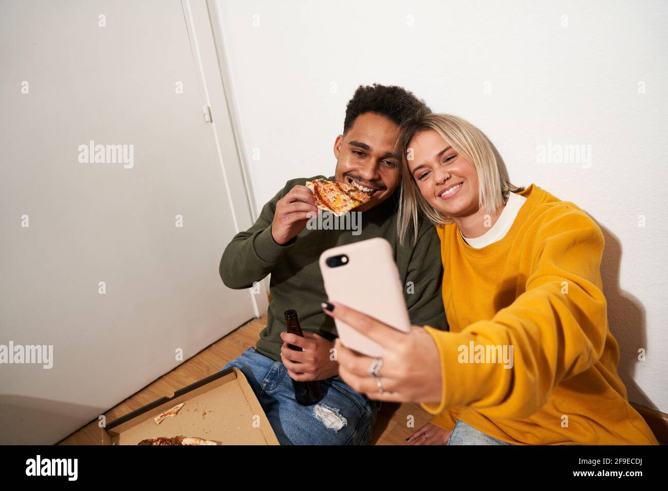 From above of positive multiracial couple eating tasty pizza and taking ...