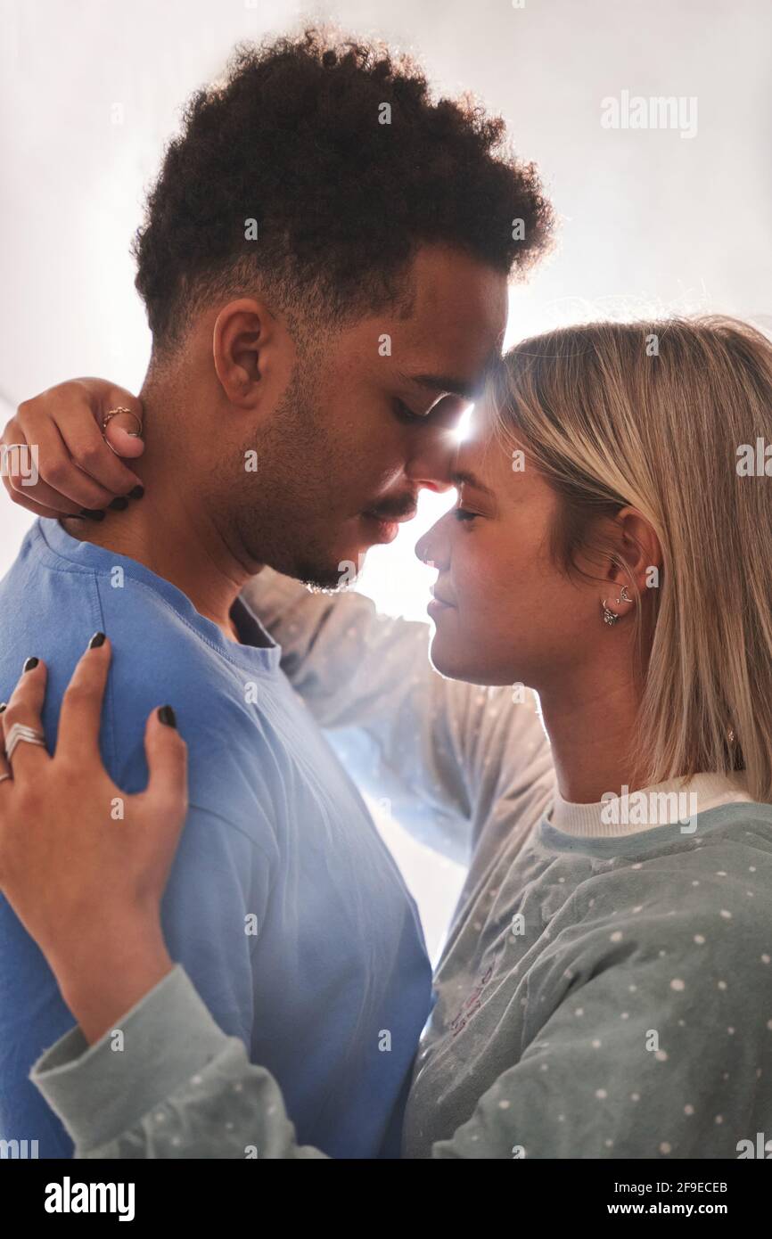 Side view of serene multiracial couple in pajamas embracing face to ...