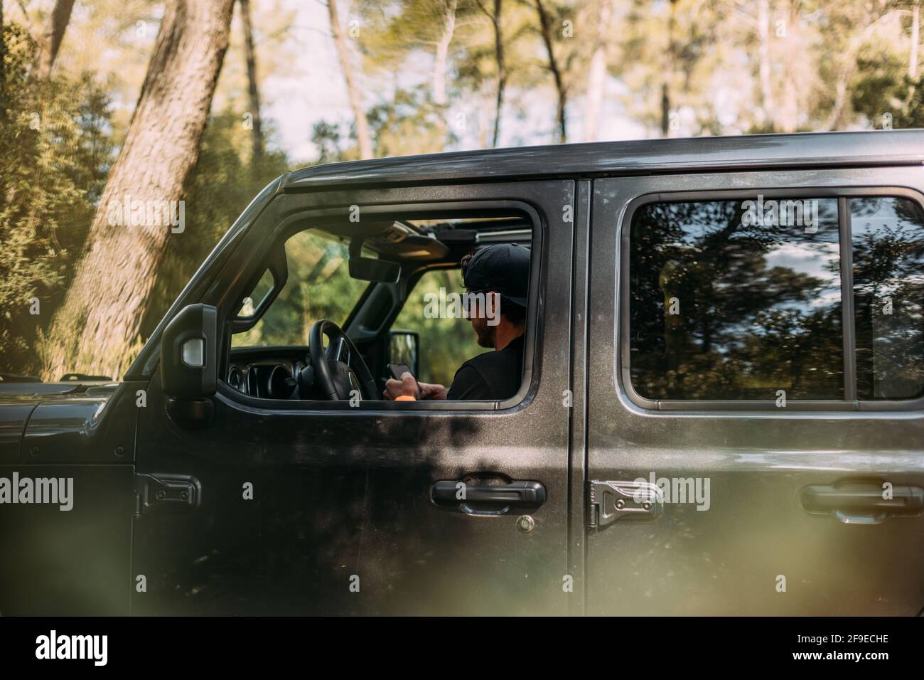 Side view of an adventurer using his smartphone inside his off-road car ...
