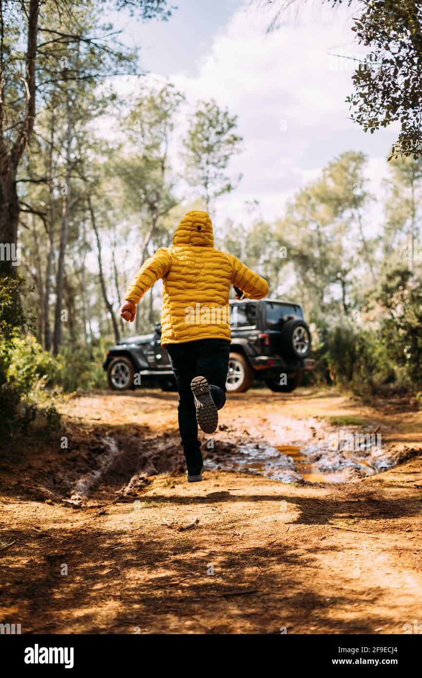 Back view of hooded adventurer running next to his off-road car on the ...