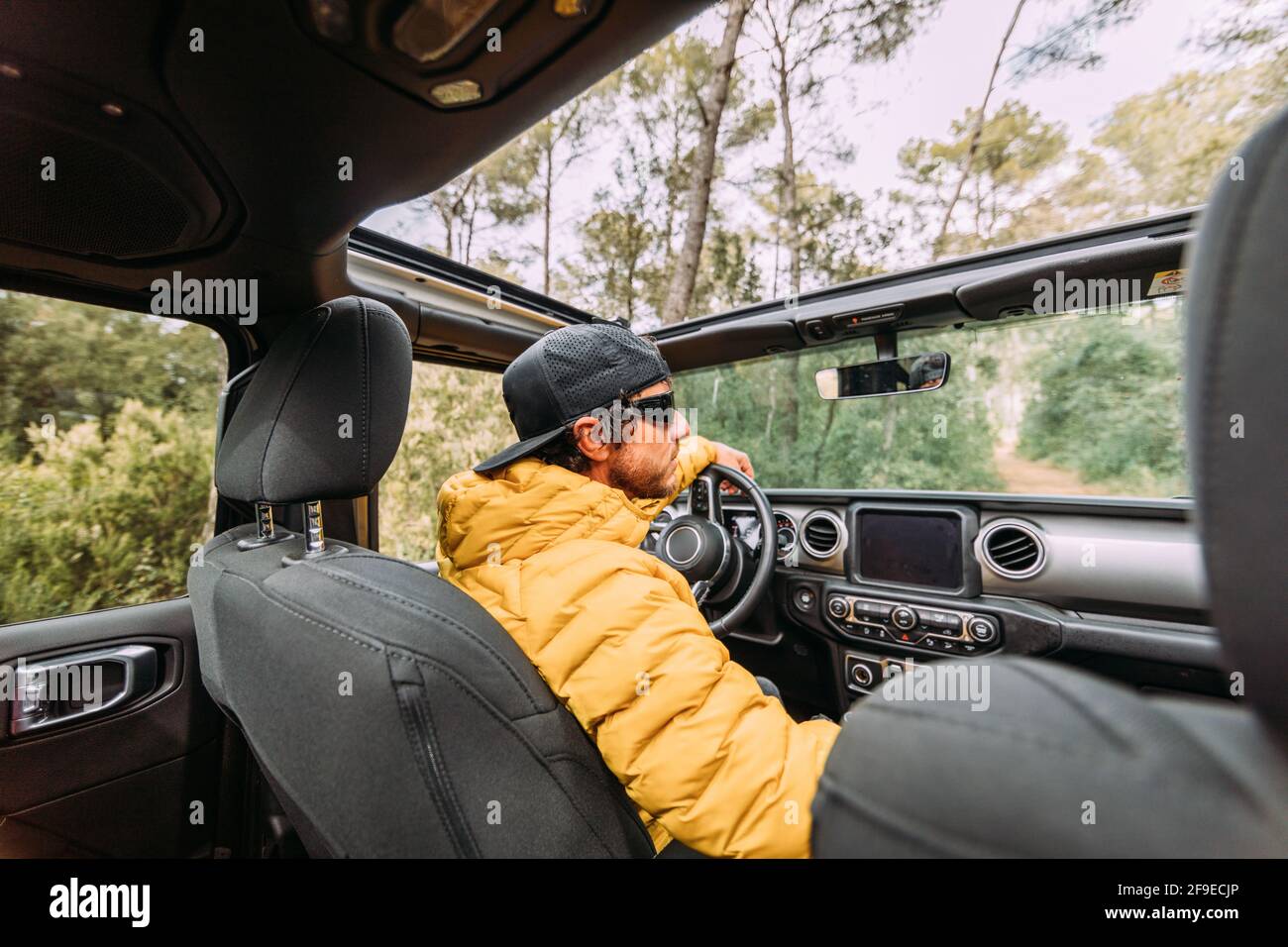 From behind inside view of a driver wearing a cap and sunglasses in an ...