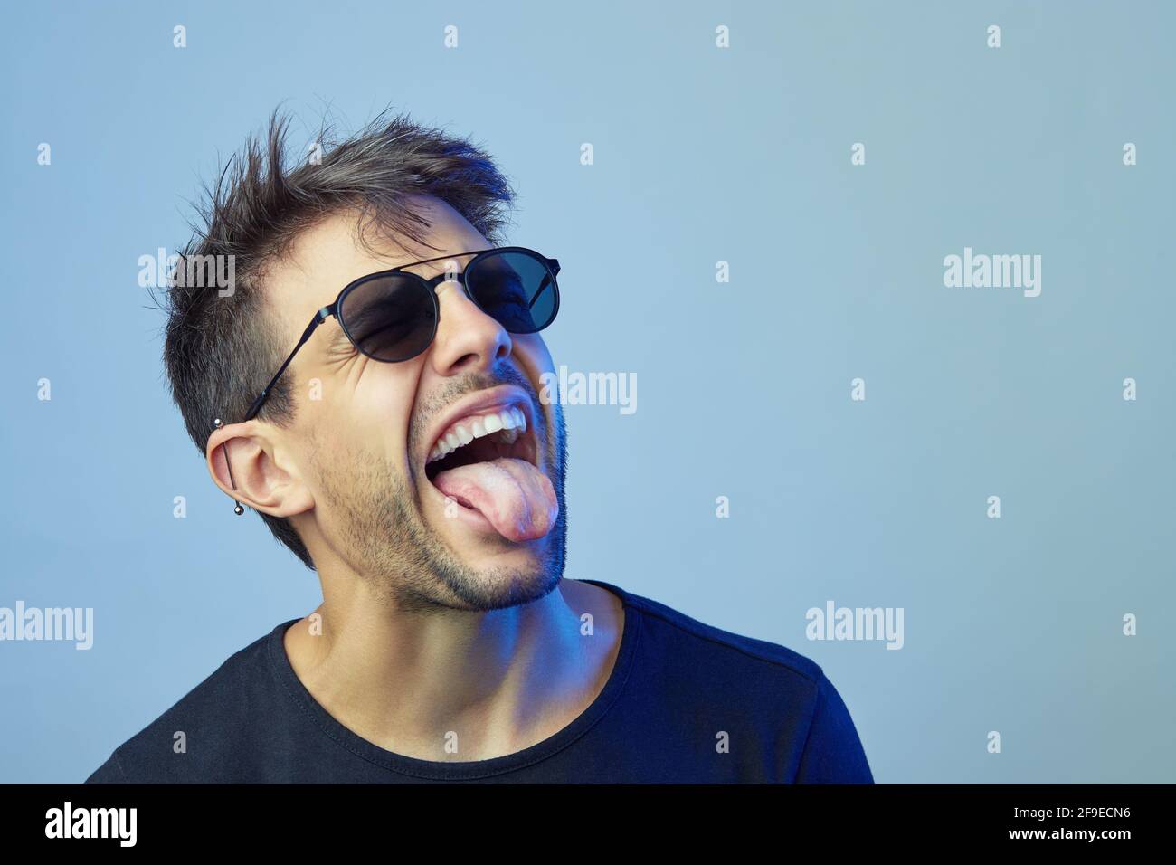 Expressive male in stylish sunglasses showing tongue and grimacing on ...
