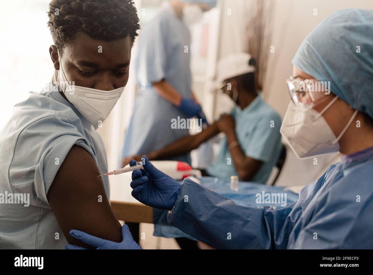 Female doctor in protective uniform and latex gloves vaccinating male ...