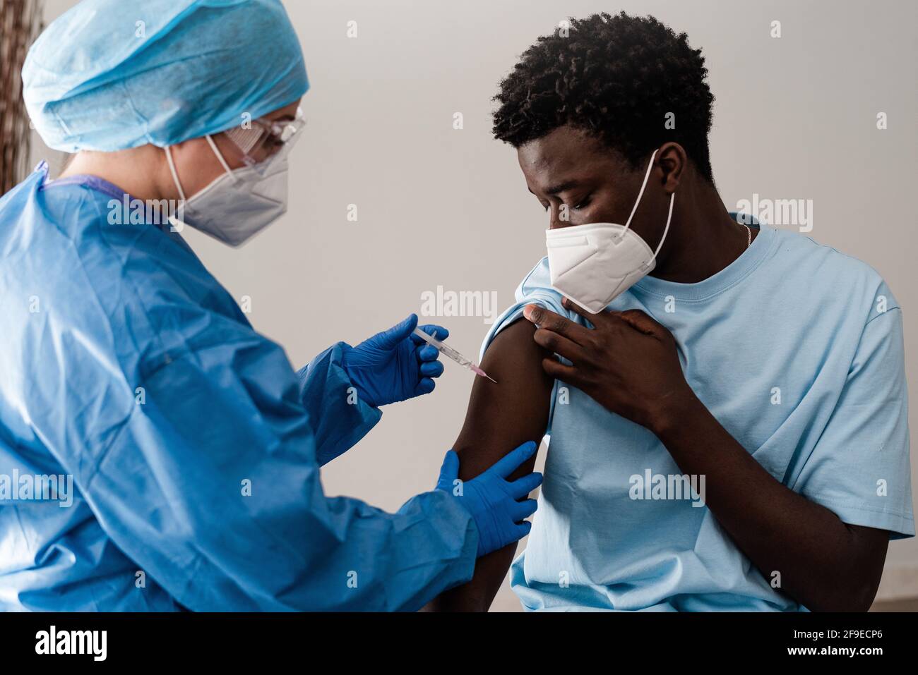 Female doctor in protective uniform and latex gloves vaccinating male ...