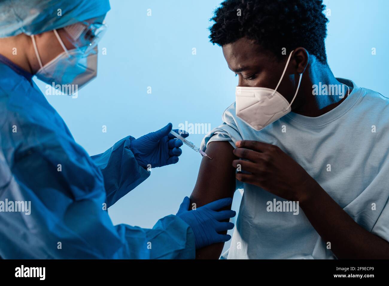 Female doctor in protective uniform and latex gloves vaccinating male ...