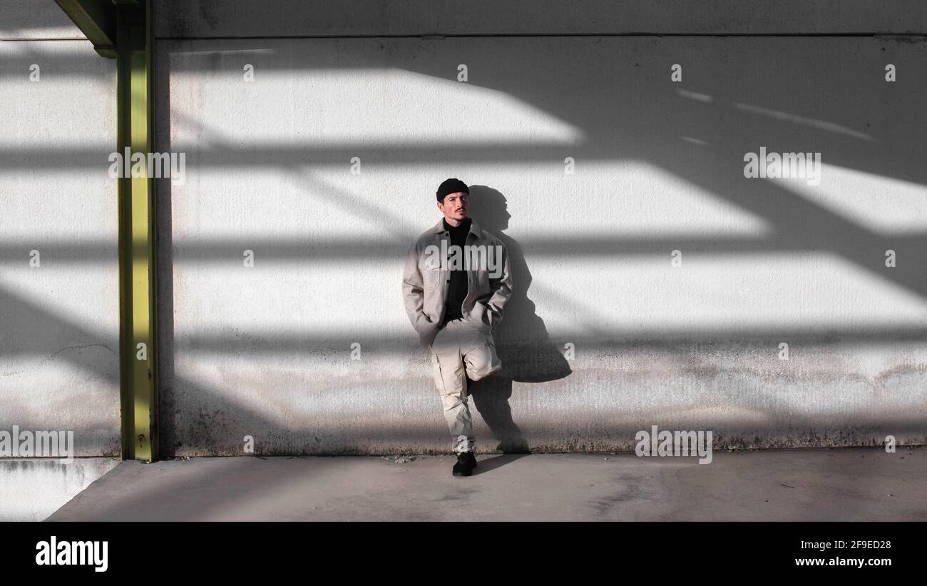 Stylish male leaning on gray shabby wall in urban area of city ...