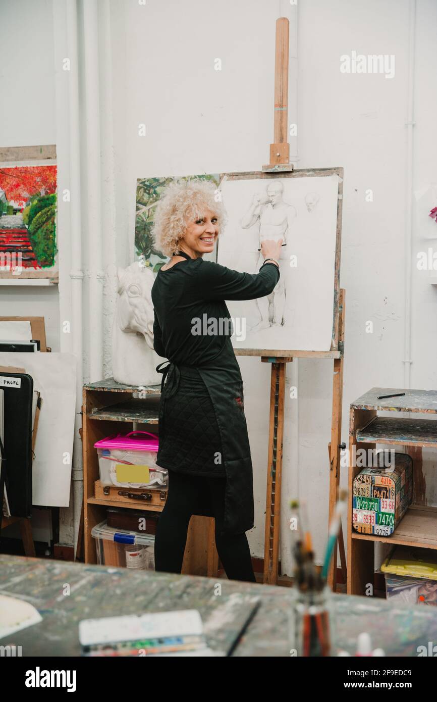 Female artist creating drawing of human with pencil while standing at ...