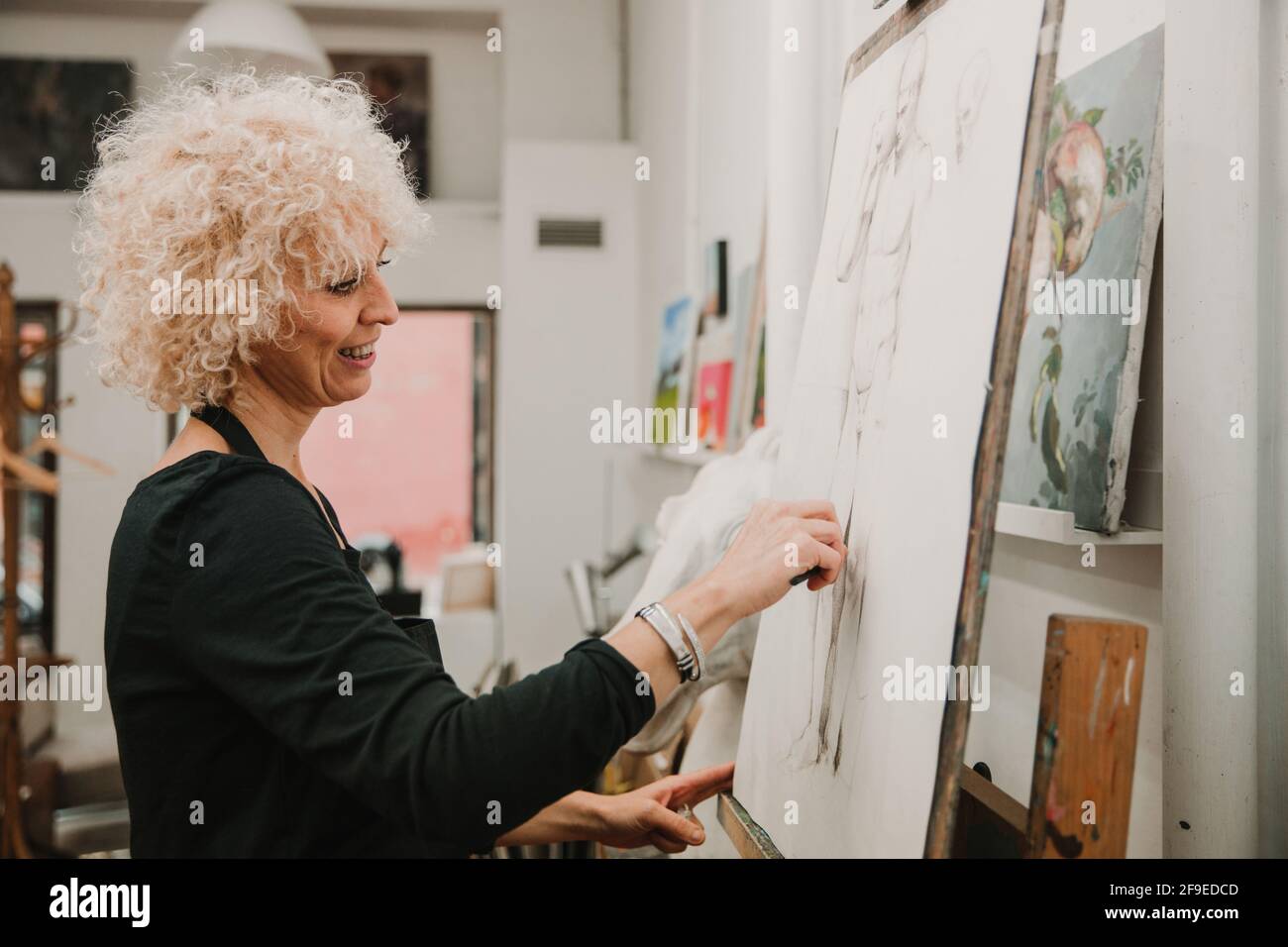 Female artist creating drawing of human with pencil while standing at ...