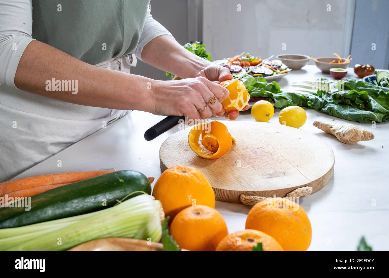 Crop anonymous female peeling fresh orange with knife over cutting ...