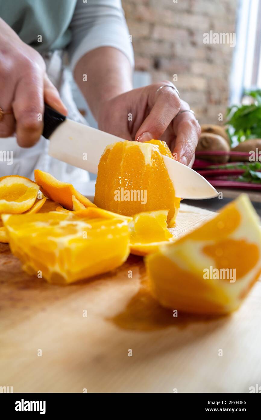 Crop unrecognizable female cutting ripe juicy oranges with knife on ...