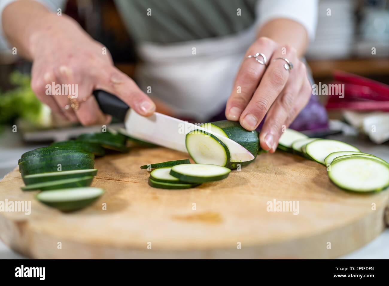 Crop unrecognizable female cutting zucchini with knife while preparing ...