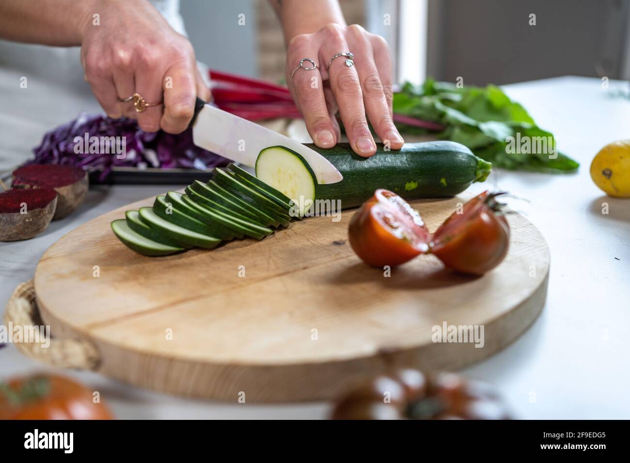 Crop unrecognizable female cutting zucchini with knife while preparing ...